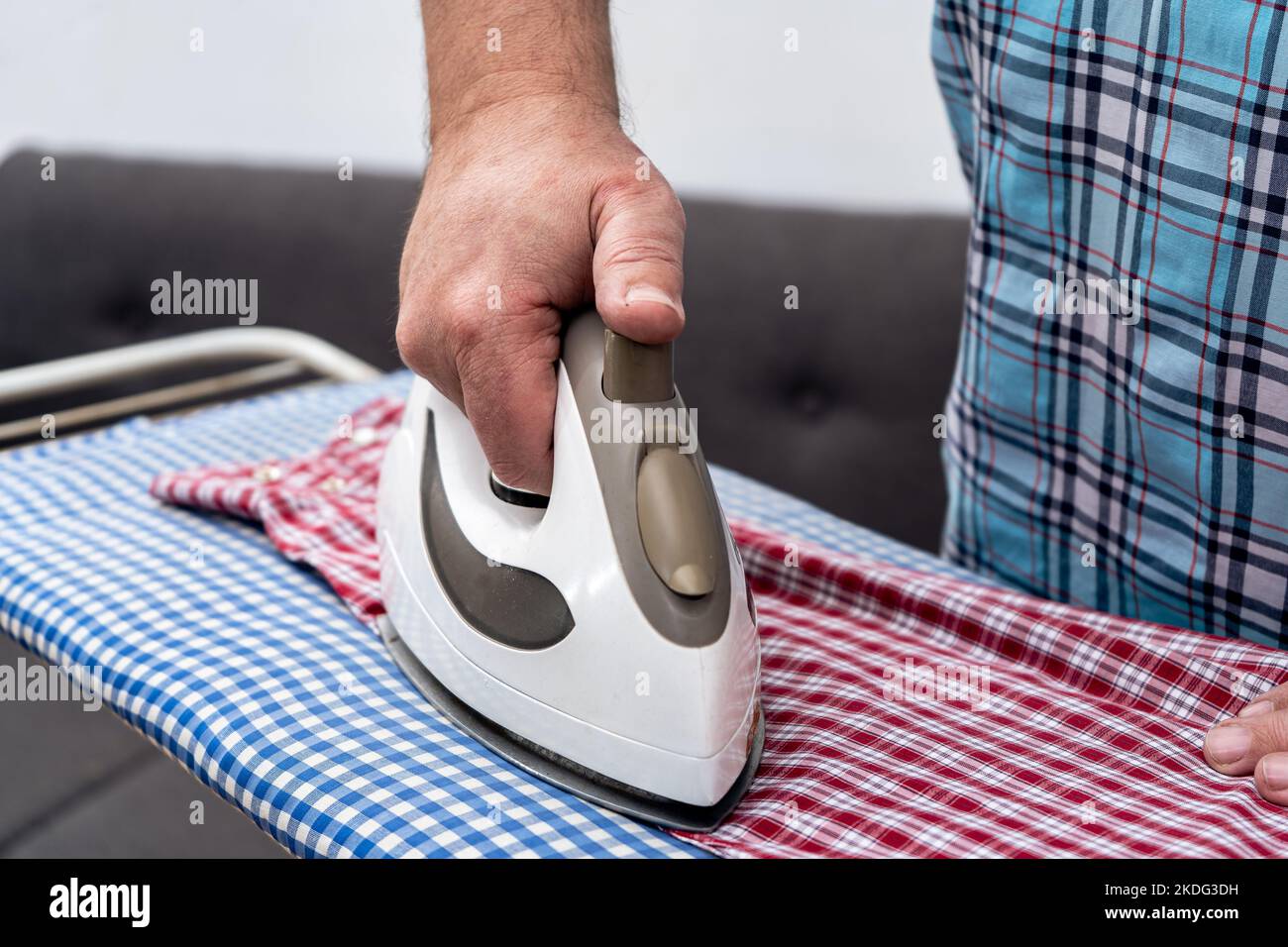 Close-up of a man's hand holding an iron while ironing a shirt on a ...