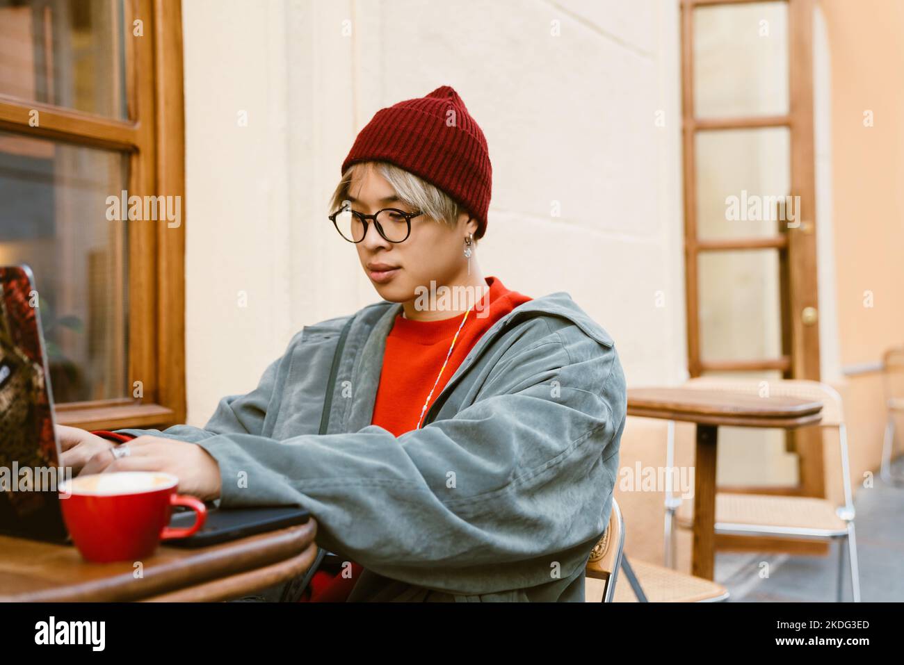 Asian boy working with laptop while drinking coffee in cafe outdoors ...