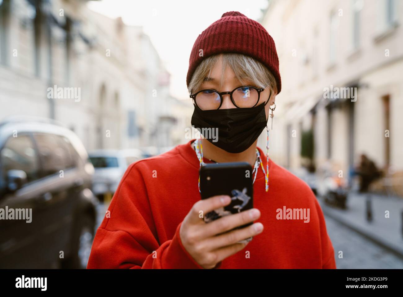 Asian boy in face mask using mobile phone while walking on city street ...