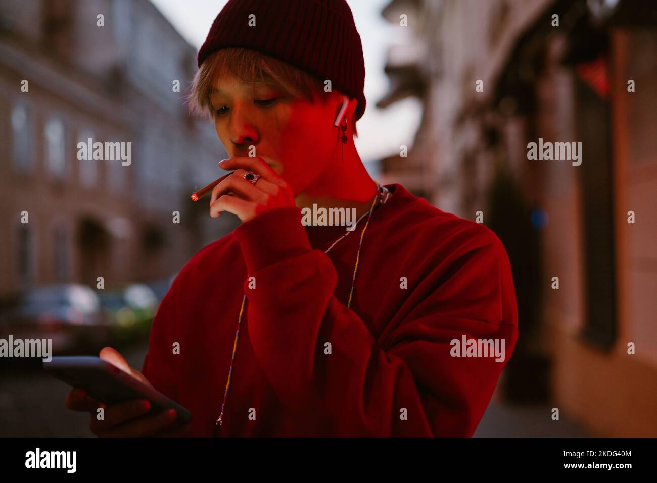 Asian boy in earphones using mobile phone while smoking at city street ...