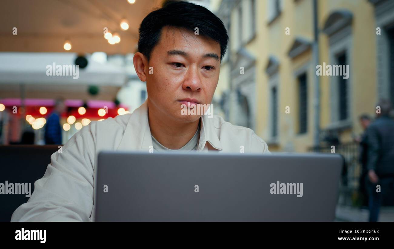 Close-up asian man sitting in cafe typing on laptop chatting online reading good message male ...