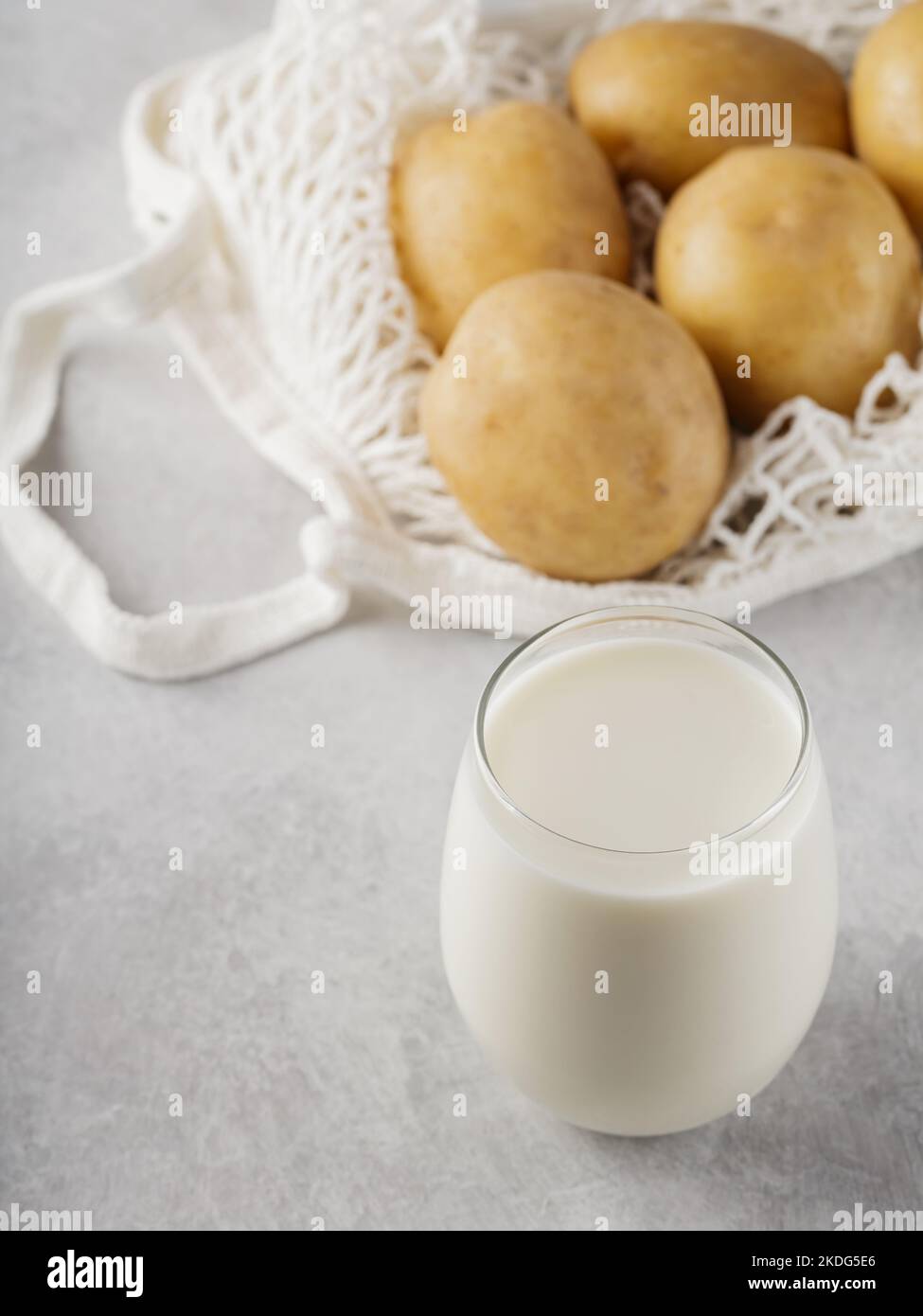 Potato milk and raw potatoes in a mesh bag. Plant based milk replacer ...