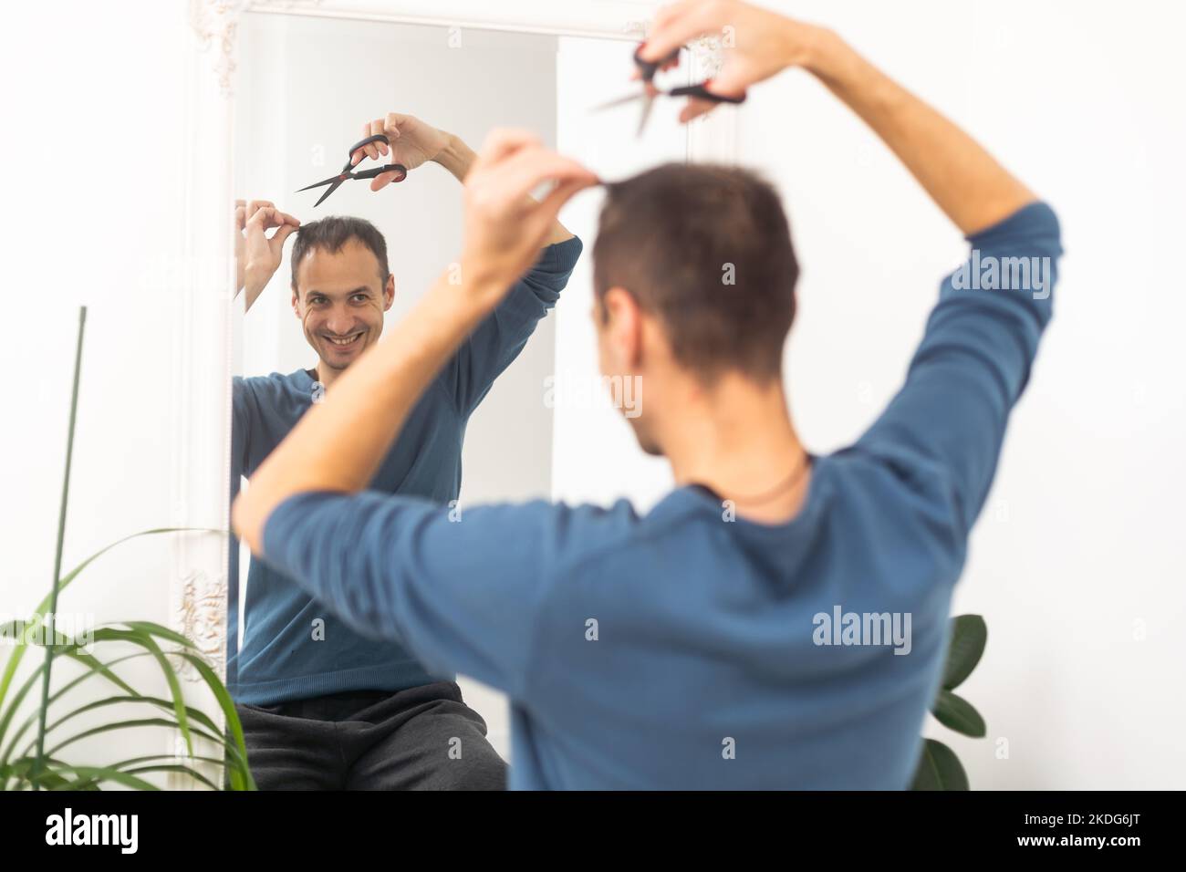 Caucasian shaggy man trying to make a haircut by himself with scissors ...