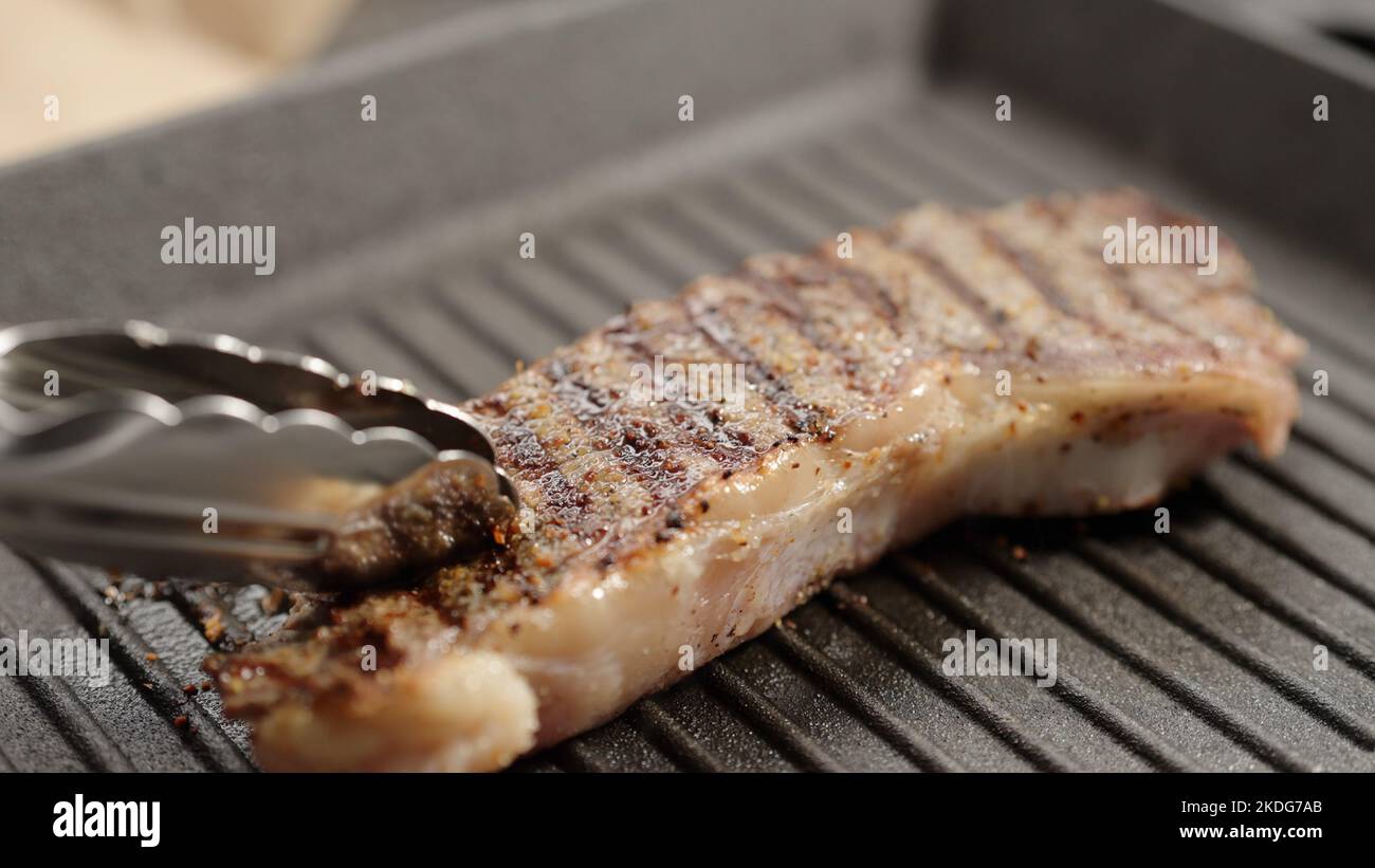 flip new york steak with tongs on grill pan, wide photo Stock Photo - Alamy