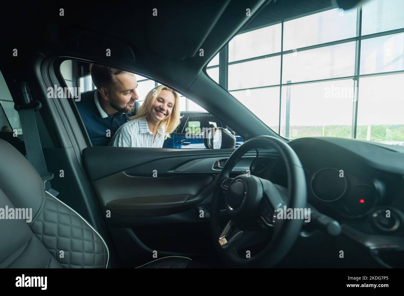 Caucasian family couple looking out the car window in a car dealership ...