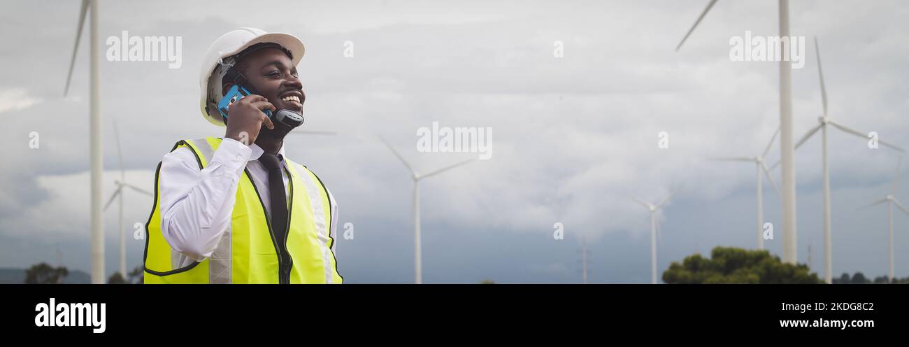 African engineer man stands using smartphone front the wind turbines ...