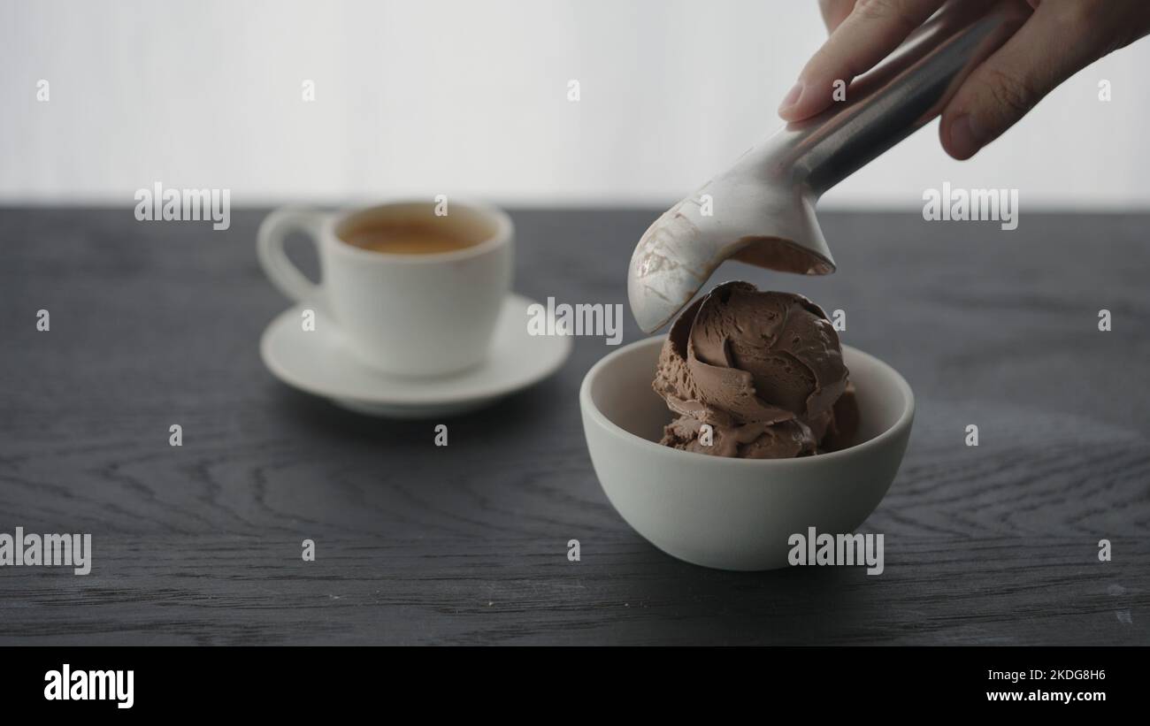Man put chocolate ice cream into white bowl next to cup of espresso ...