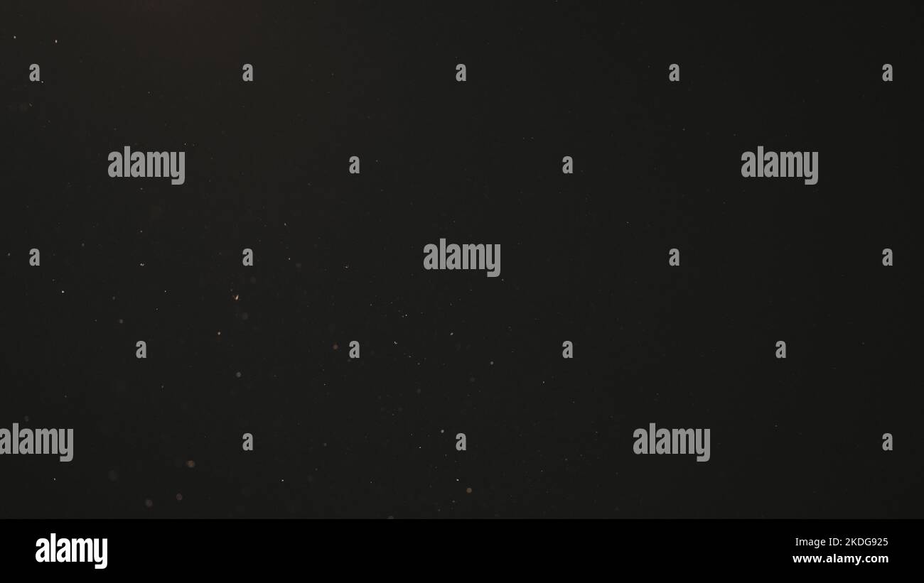 Slow motion dust particles float in warm light on black background ...