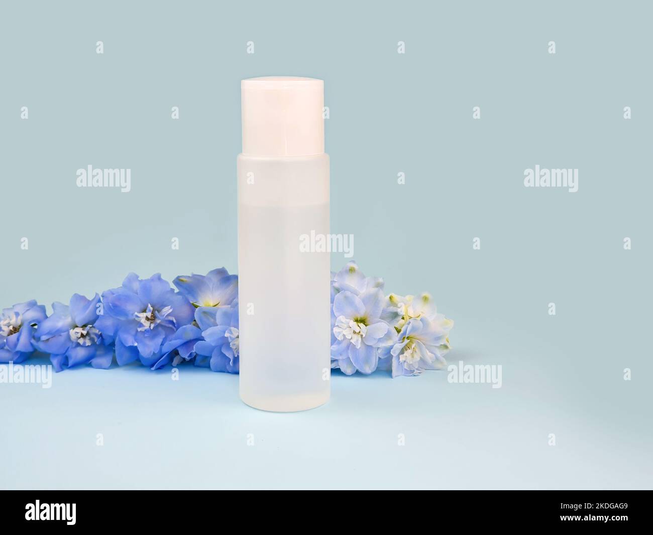 Bottle with clear micellar water and blue delphinium flower on a blue ...