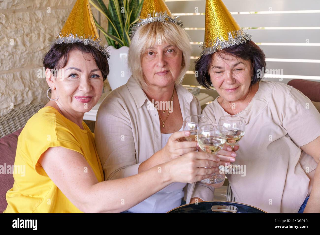 Happy senior women wearing party hats drinking wine together at ...
