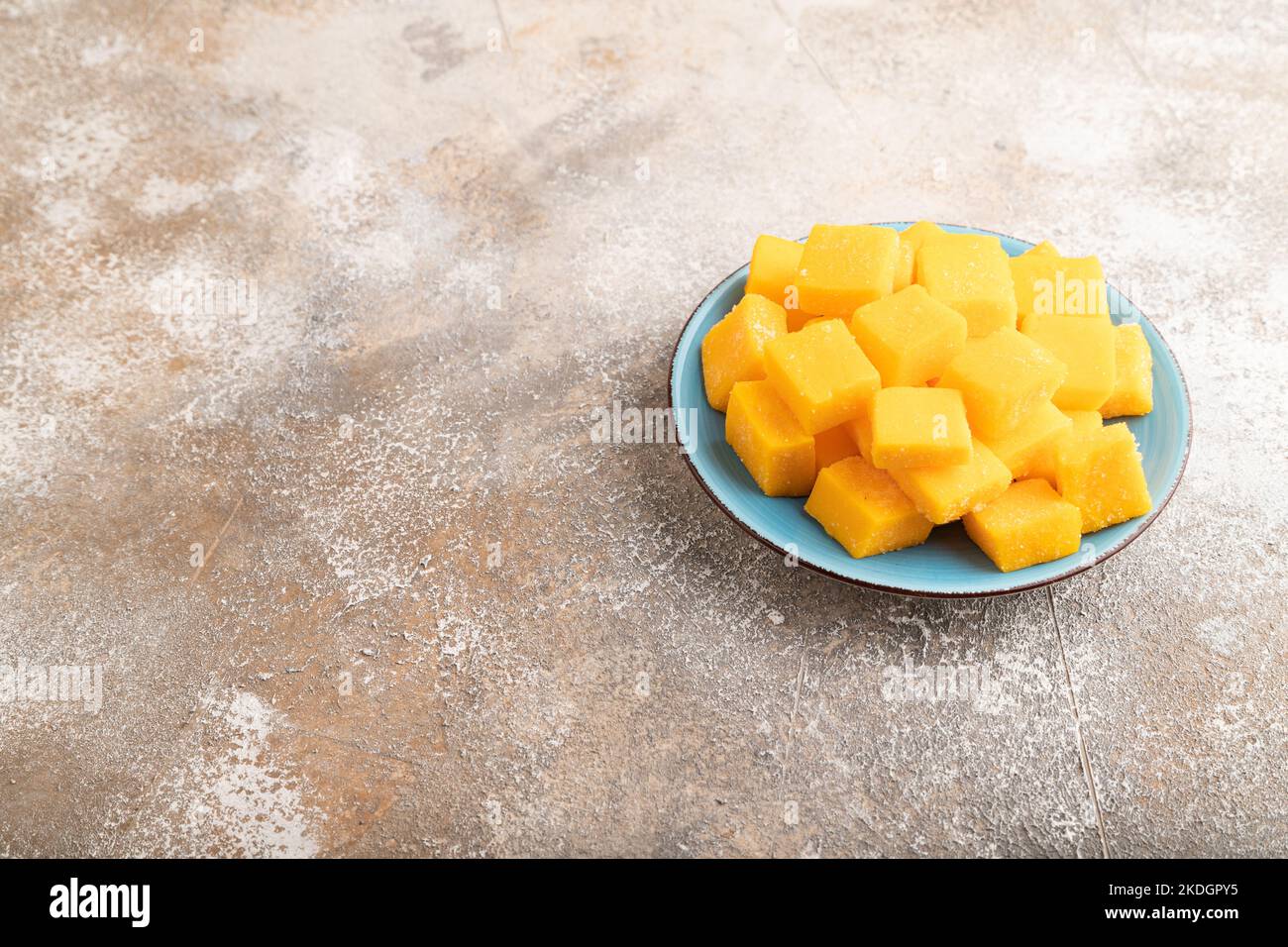 Dried and candied mango cubes on blue plate on brown concrete ...