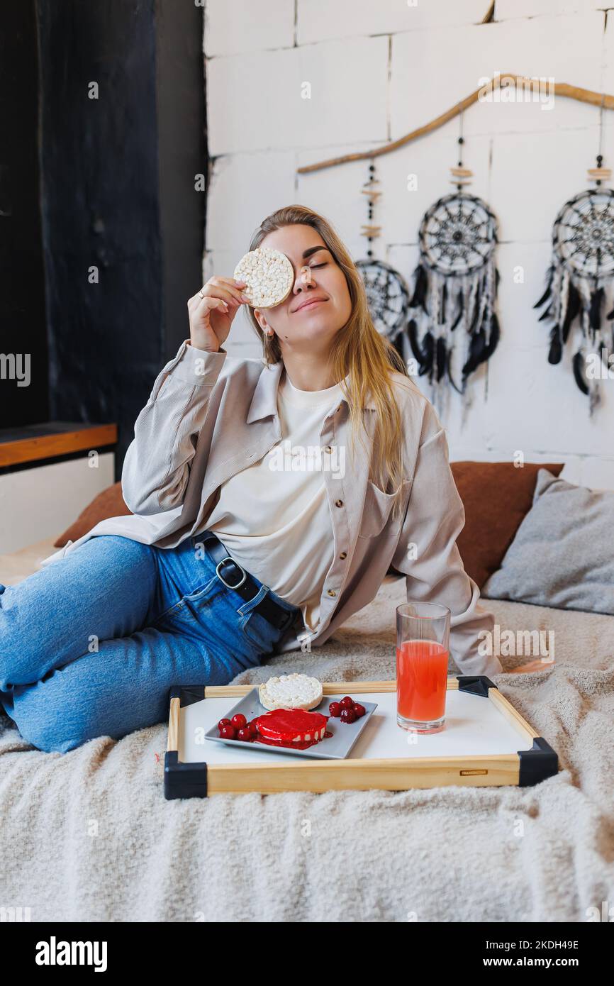 A young slender woman is sitting on the bed and eating a delicious ...