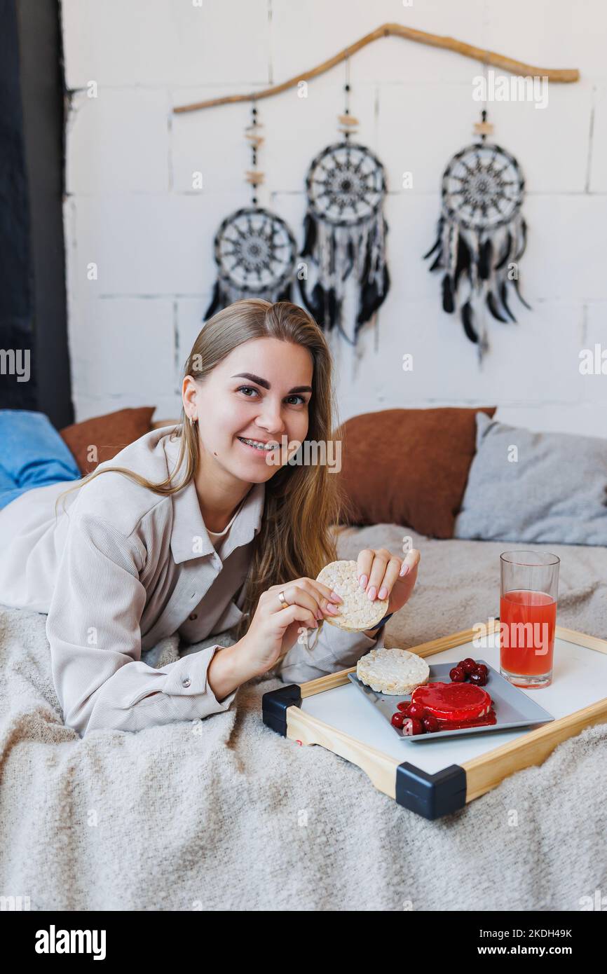 A young slender woman is sitting on the bed and eating a delicious ...