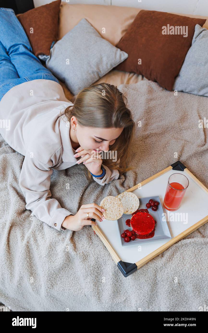 A young slender woman is sitting on the bed and eating a delicious ...