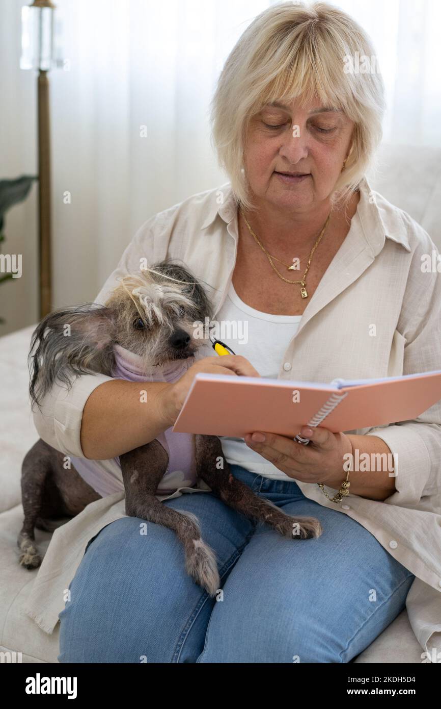 Older caucasian woman writing notes in notebook planner, sitting with ...