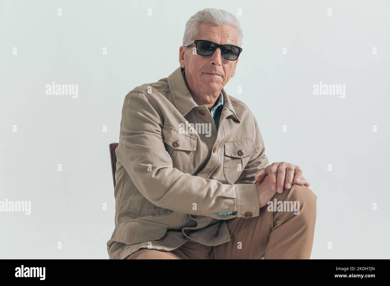 Cool businessman in his 60s sitting on a wooden chair, resting his ...