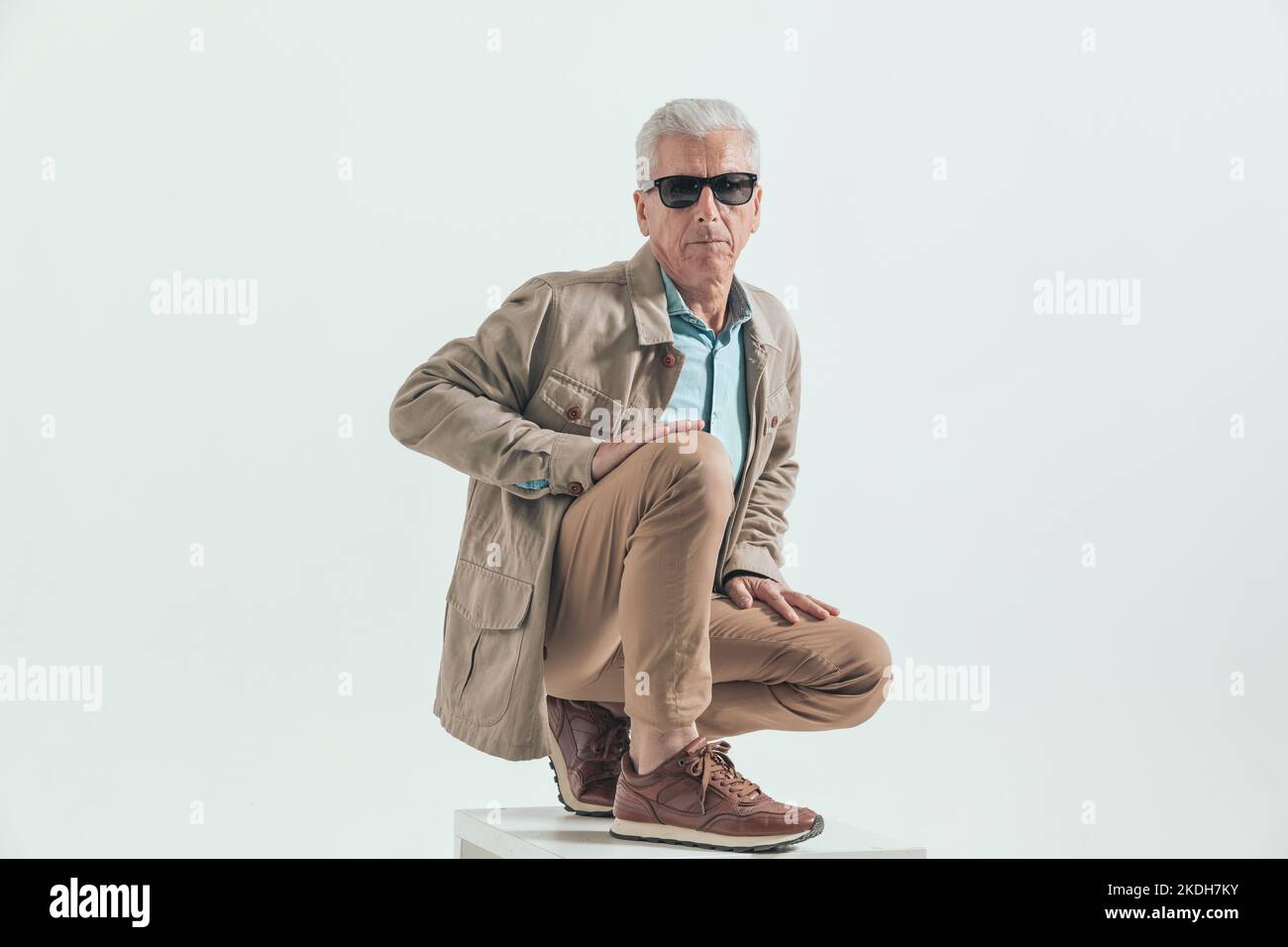 cool business man in his 60s squatting on the chair and wearing ...