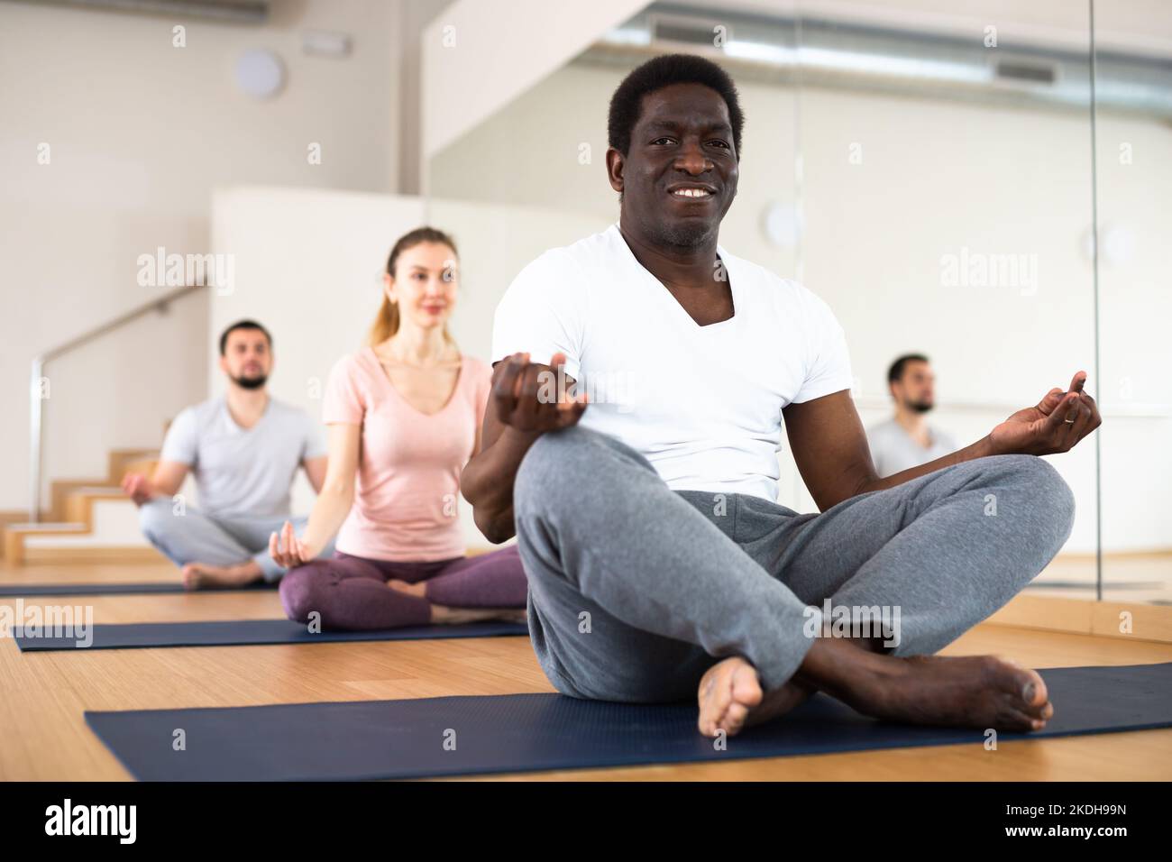 Smiling african american man sitting in lotus pose in fitness room ...