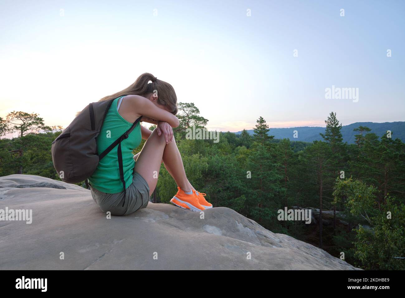 Lonely young woman sitting depressed on hillside trail on warm summer ...