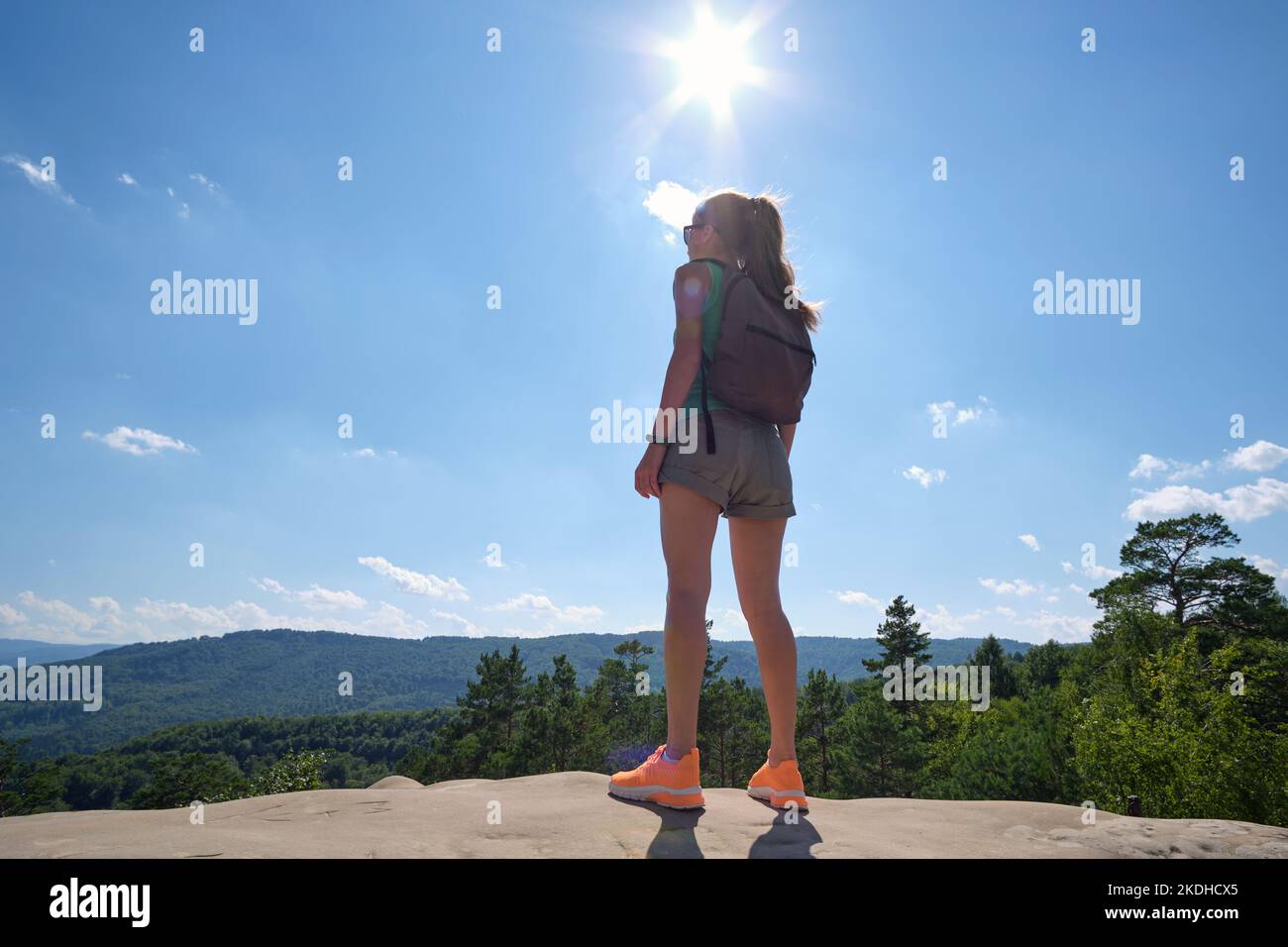 Sportive woman standing alone on hillside trail on hot day. Female hiker enjoying view of summer ...