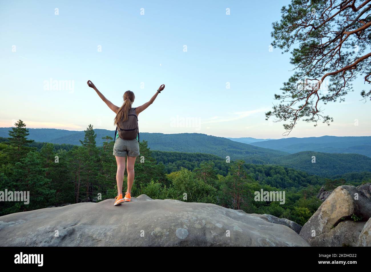 Sportive woman standing alone on hillside trail with raised up arms. Female hiker enjoying view ...