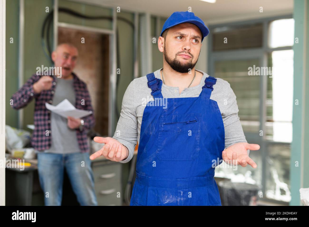 Perplexed builder in building under renovation with screaming customer ...