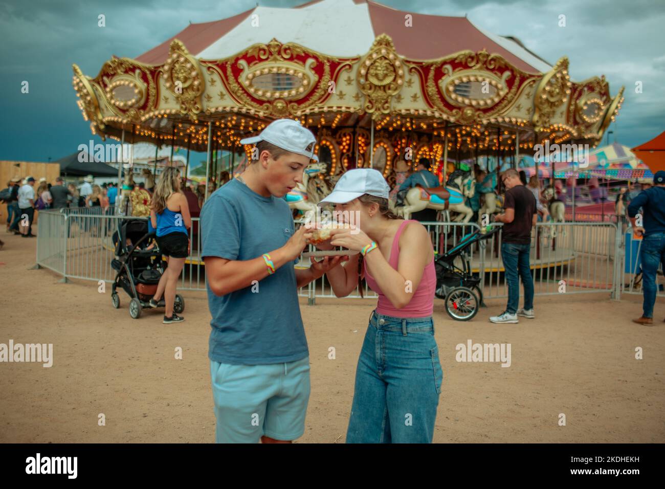 Two teenagers eating a funnel cake in front of a carousel Stock Photo ...