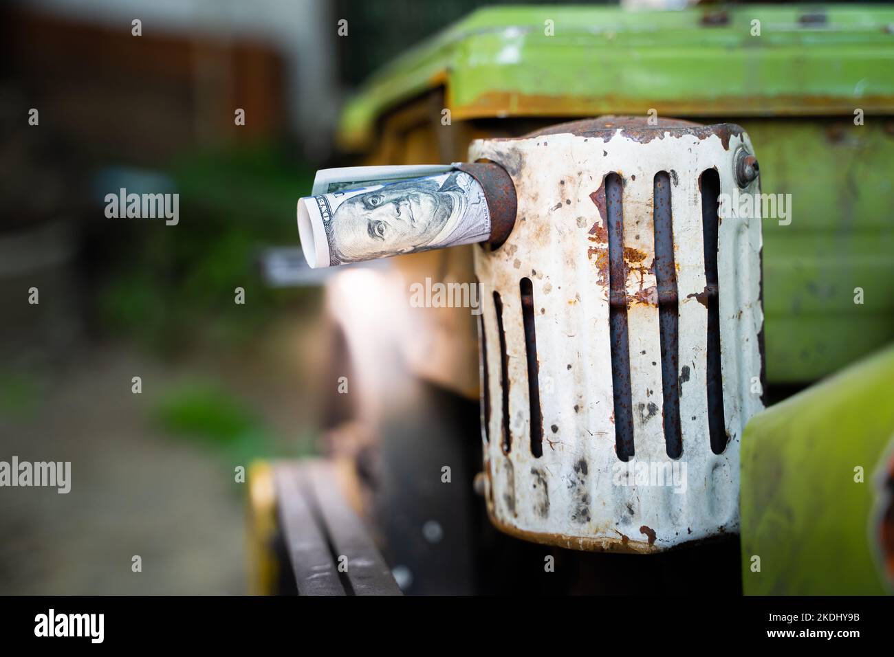 A hundred dollar bill covers the exhaust pipe of a mini tractor. Money ...