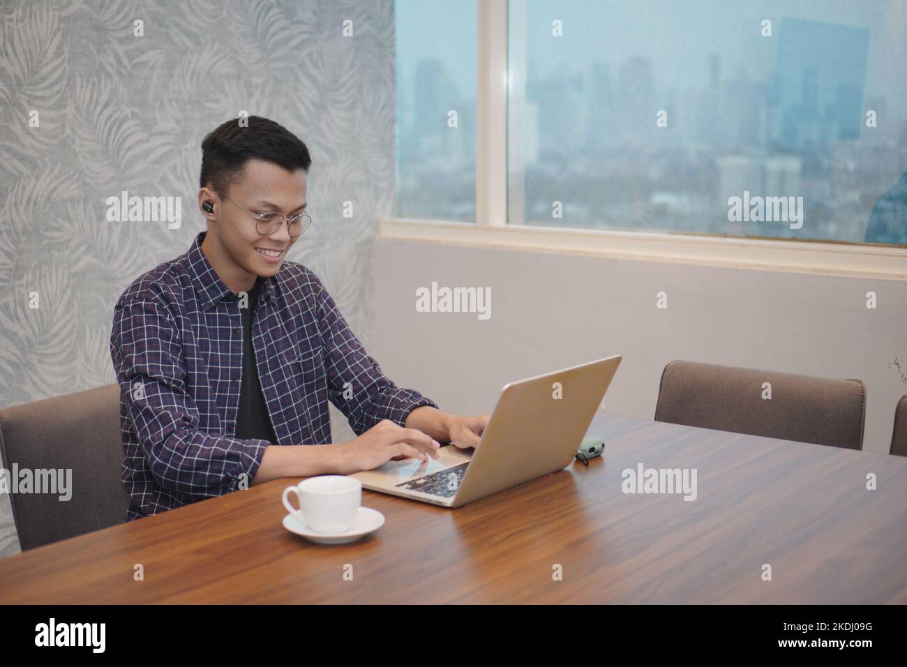 Young man smiling while working on laptop in modern office space ...