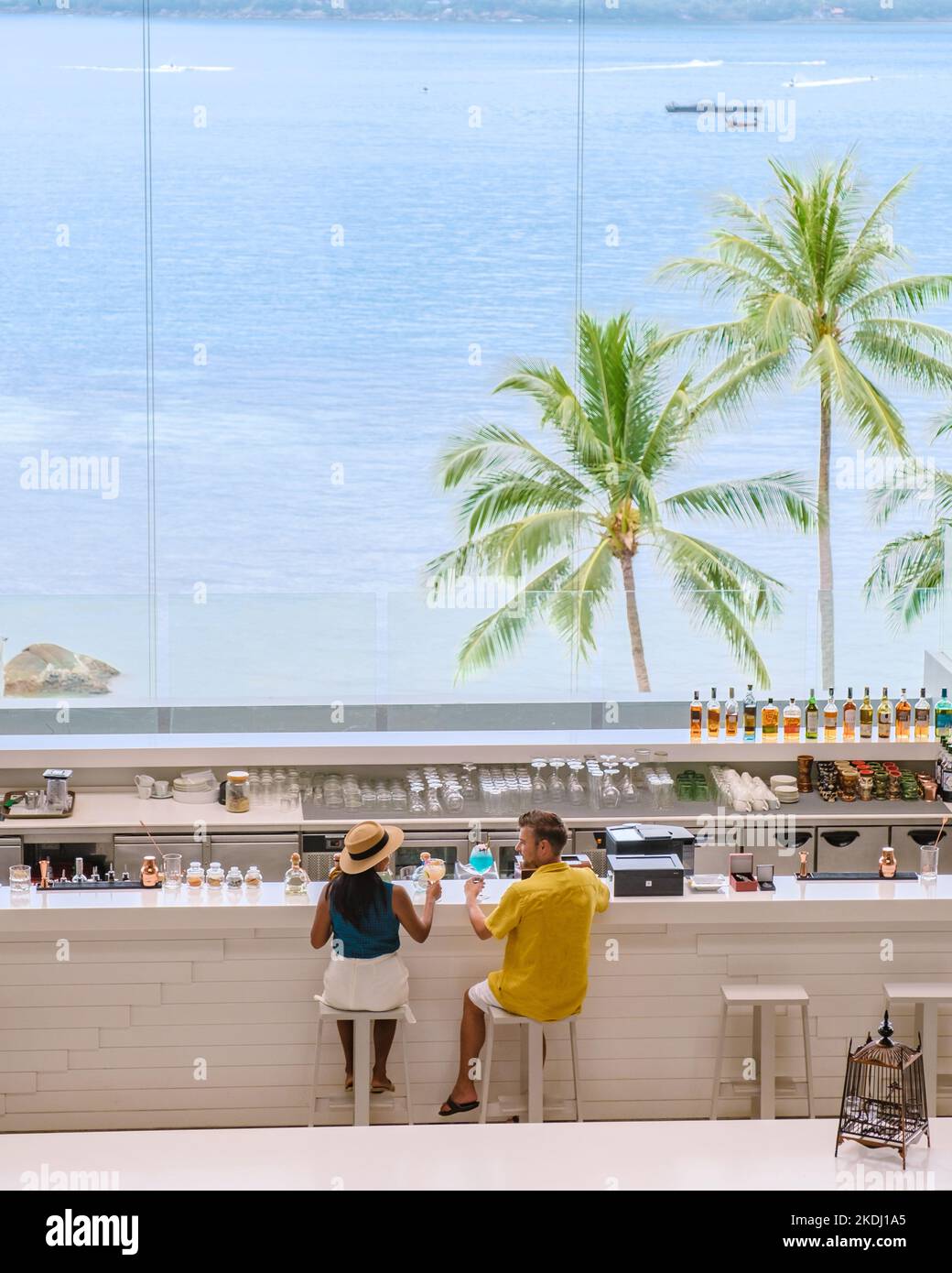 couple drinking cocktails at a bar during vacation looking out over the ...