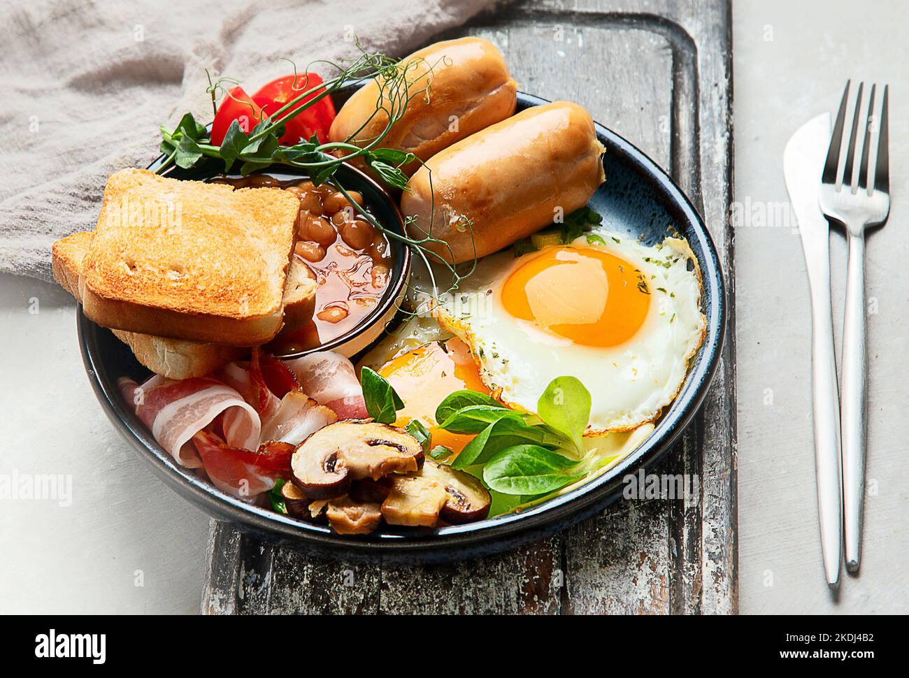 Full English breakfast with fried egg, sausage, bacon and toast on grey ...