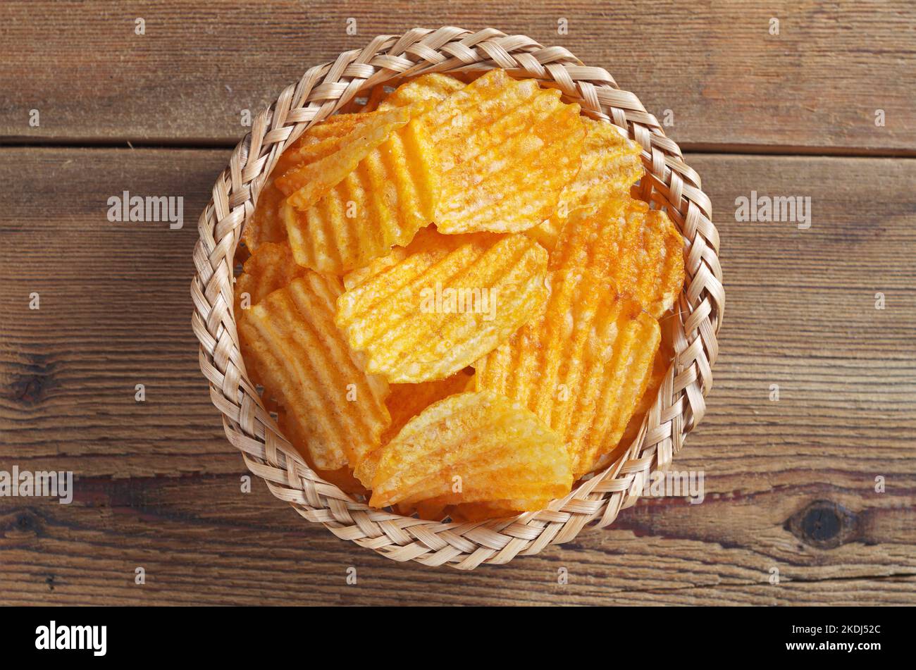 Salty ribbed potato crisps in a wicker bowl on the wooden table, top ...