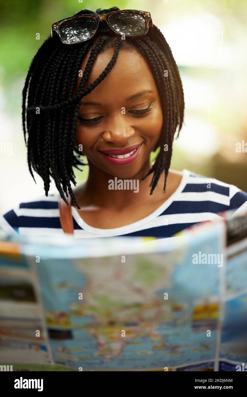 Finding her way old school. a smiling young woman reading a map while ...