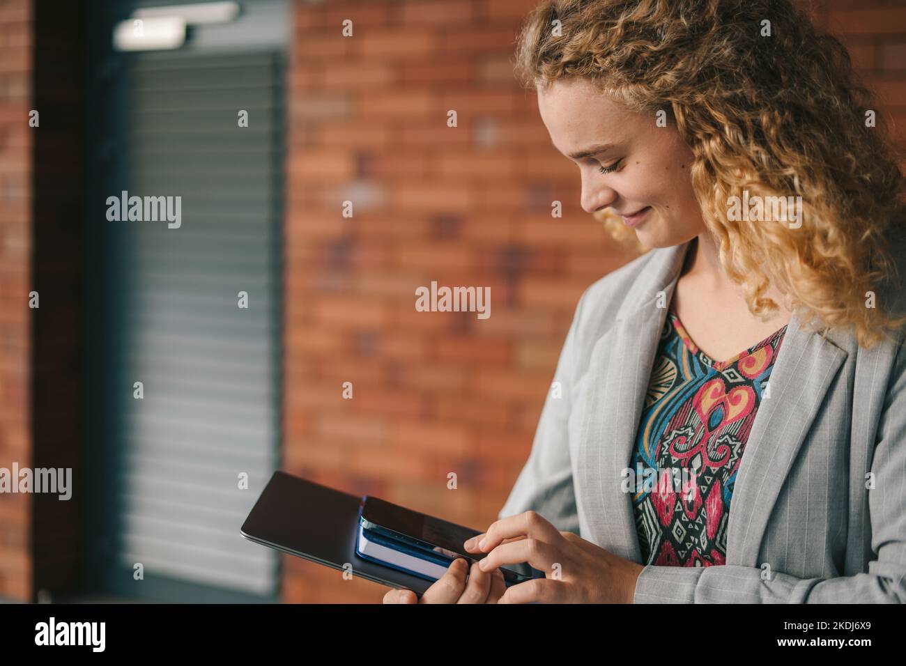 Young caucasian curly-haired woman smiling happy using smartphone at ...