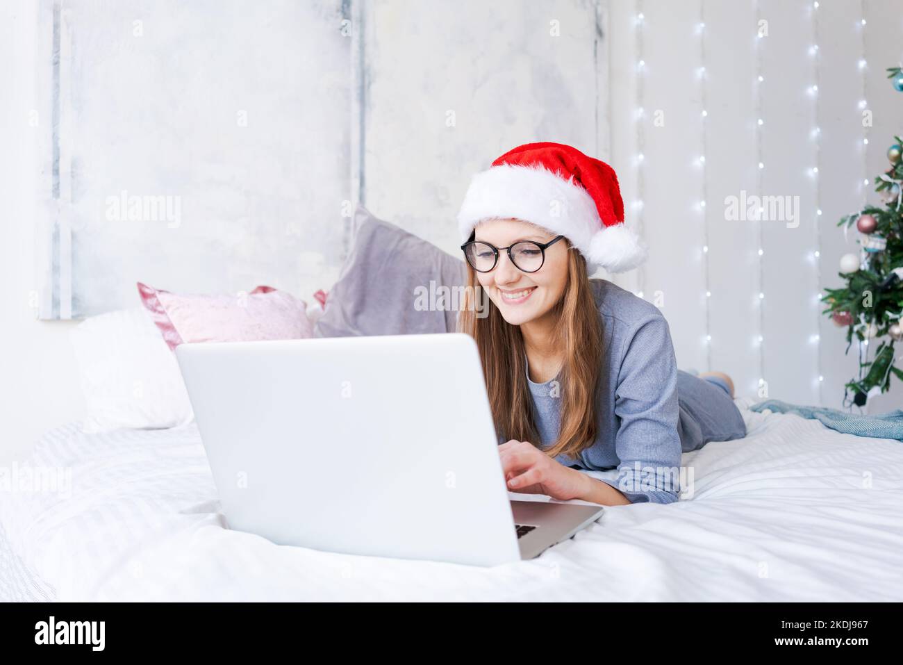 Happy girl in santa hat shopping online on laptop and sitting on bed ...