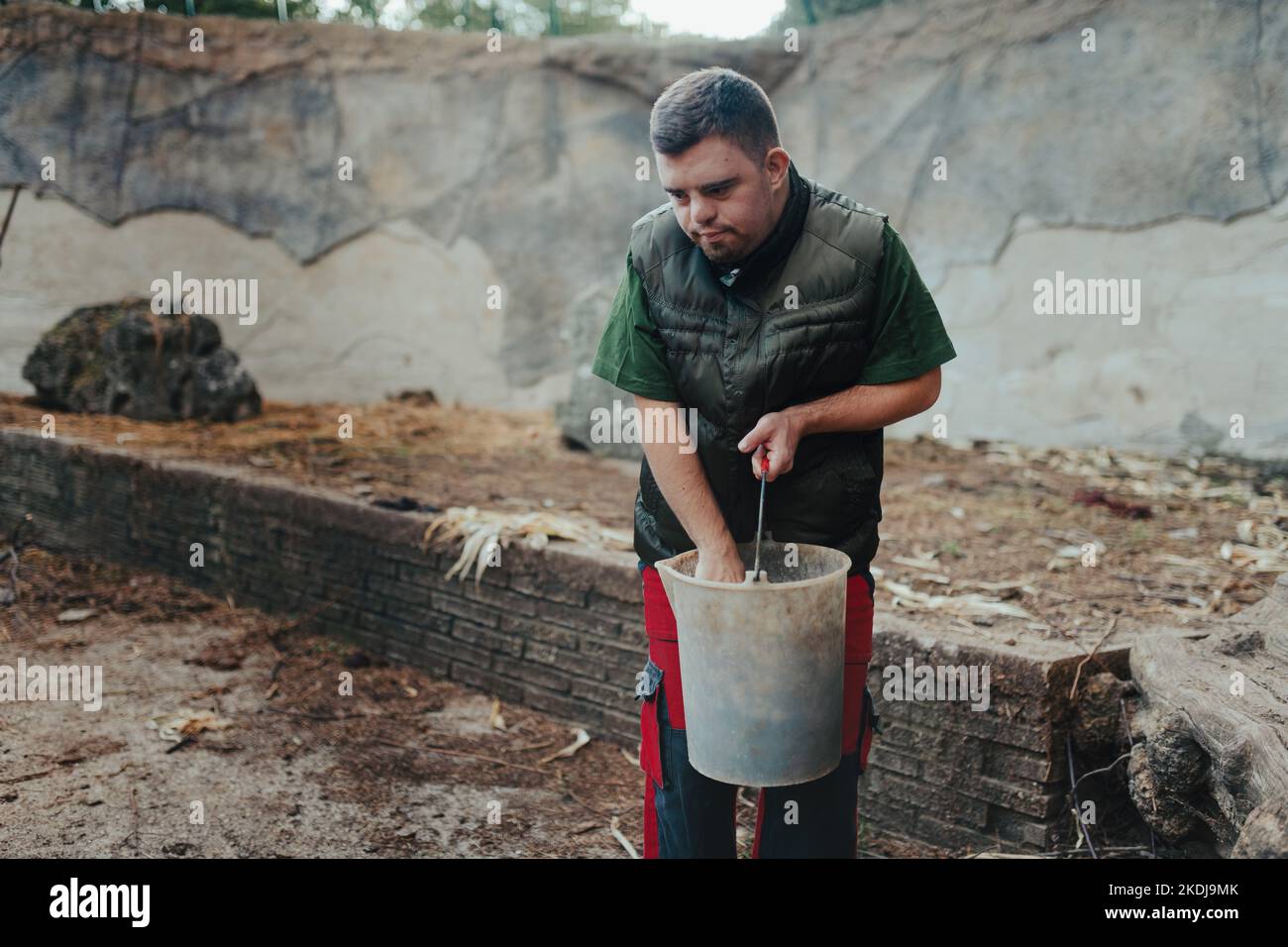 Caretaker with down syndrome in zoo giving food in animal enclosure ...
