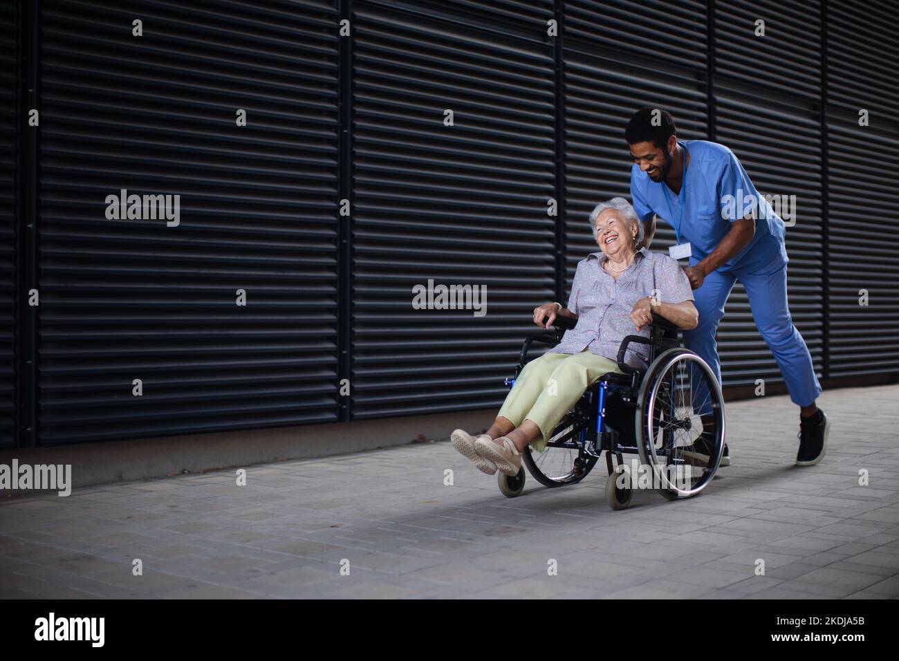 Caregiver man pushing excited senior woman at wheelchair on the street ...