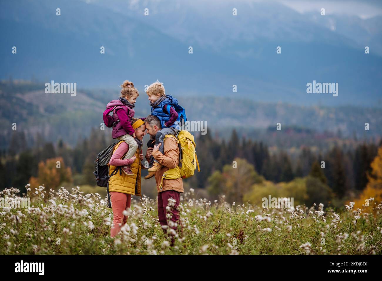 Happy parents with their little kids on piggyback at autumn walk, in ...