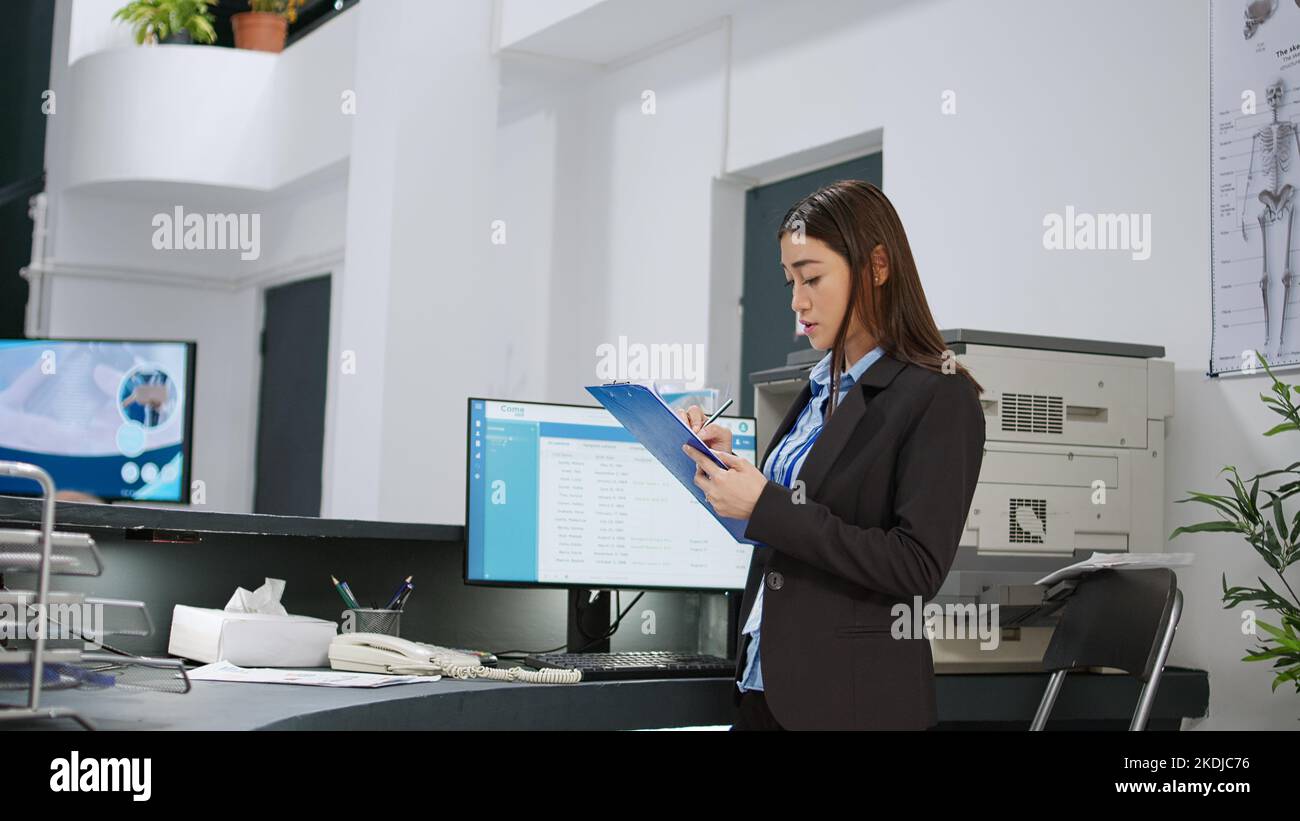 Asian receptionist taking notes on report papers to help with insurance ...