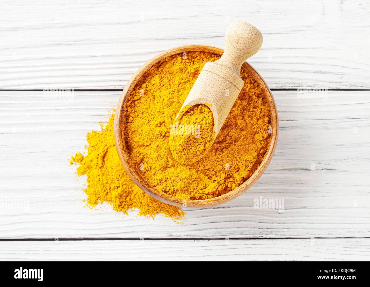 Dry turmeric (curcuma) powder in wooden bowl with scoop on white wooden ...