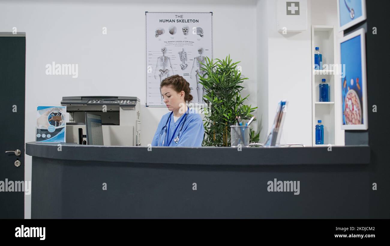 Nurse using computer to make checkup appointments at reception desk ...