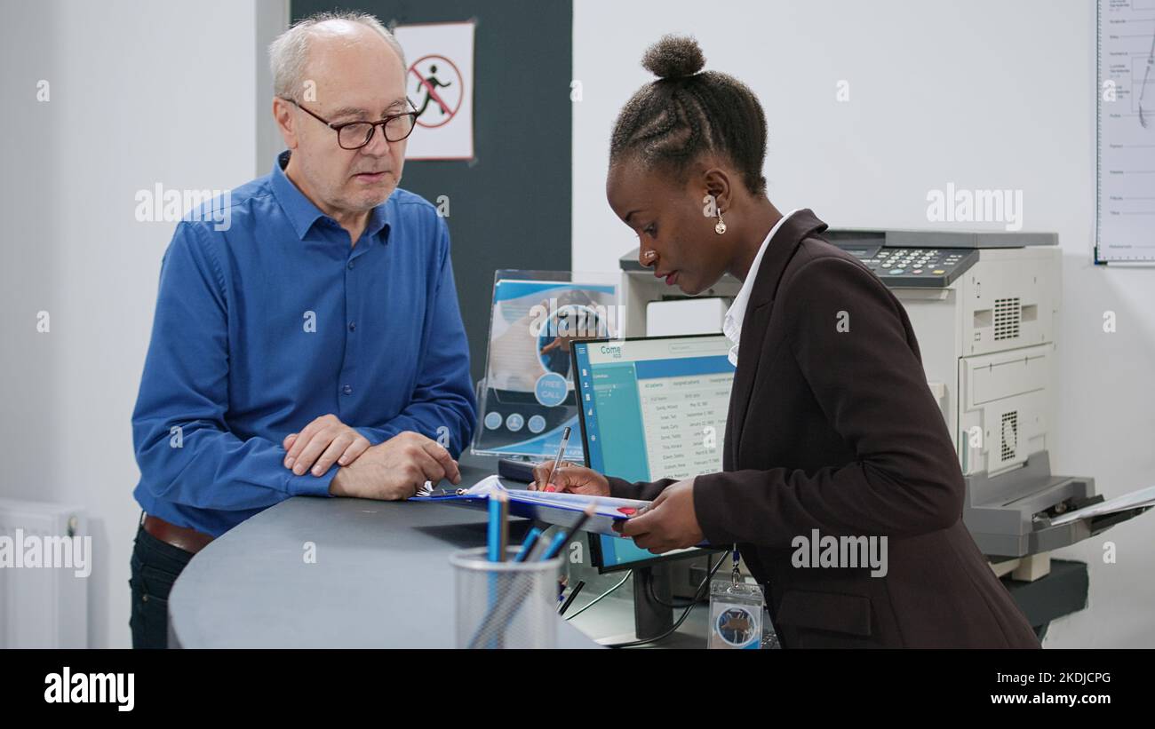 Receptionist and senior patient talking about medical report and ...