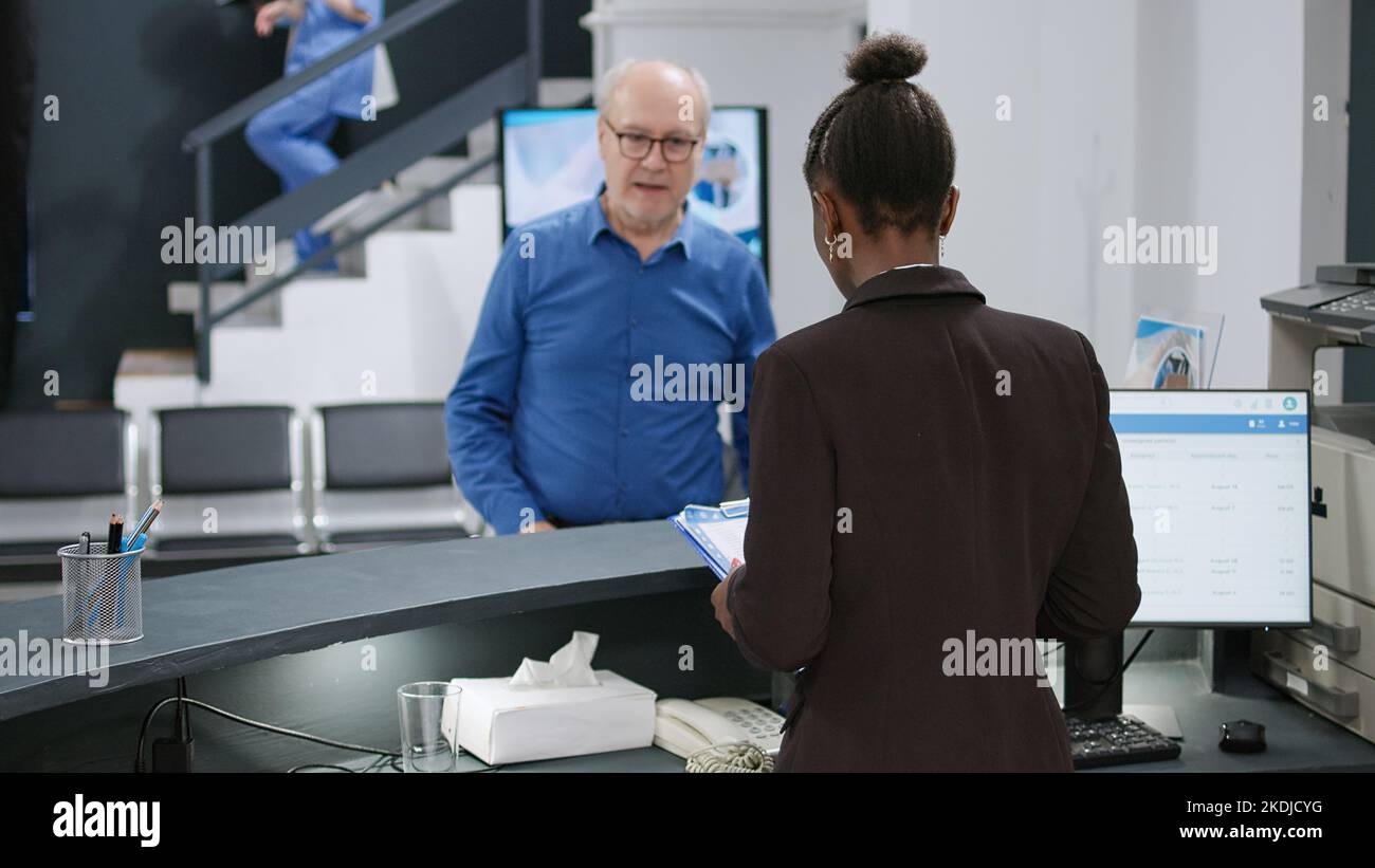 Senior man filling in appointment form papers at hospital reception ...