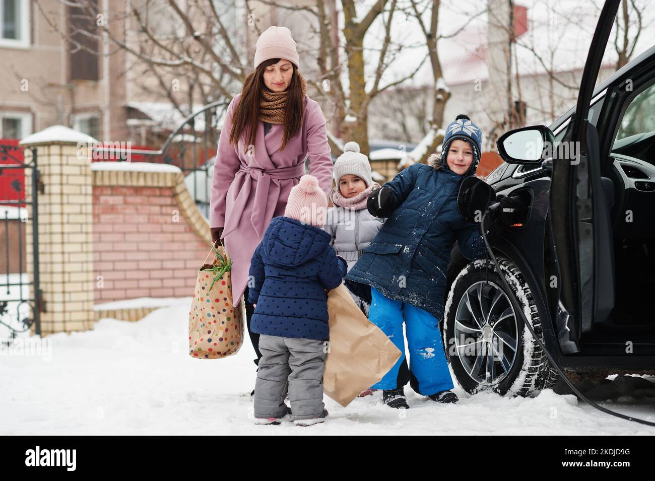 Young woman with children hold eco bags and charging electric car in ...