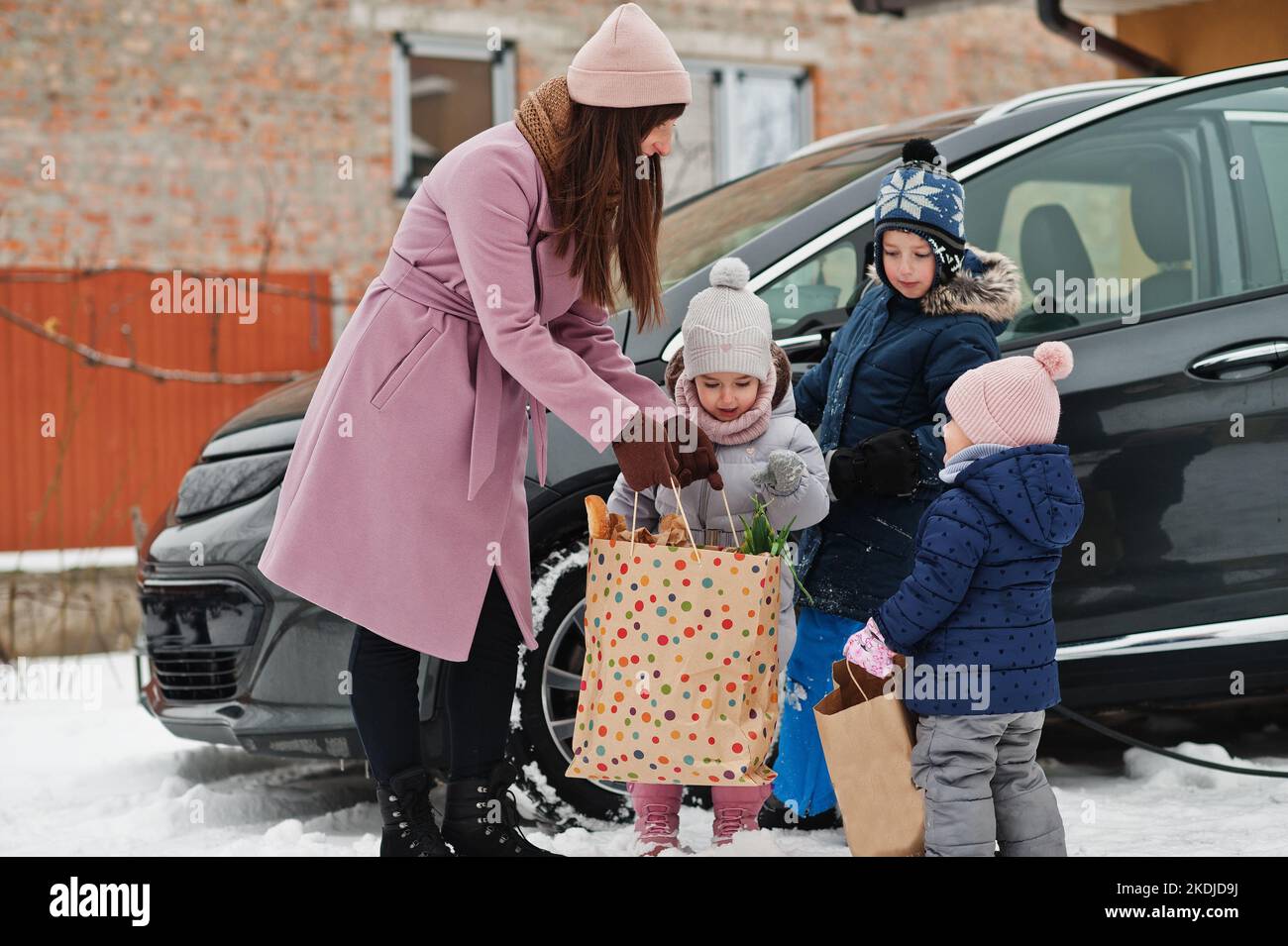 Young woman with children hold eco bags and charging electric car in ...