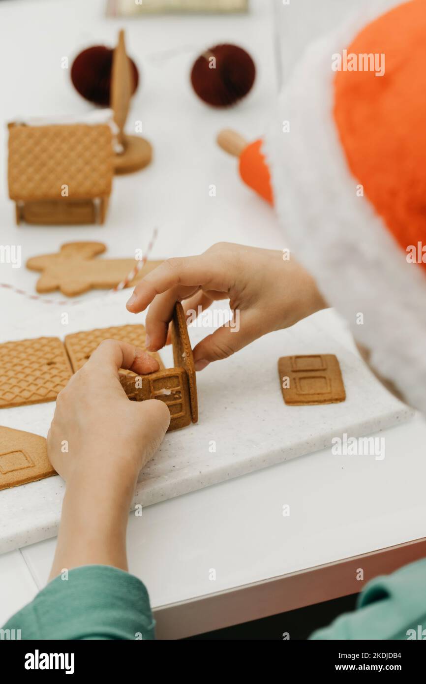 A child in a Santa hat makes a gingerbread gingerbread house. New Year ...