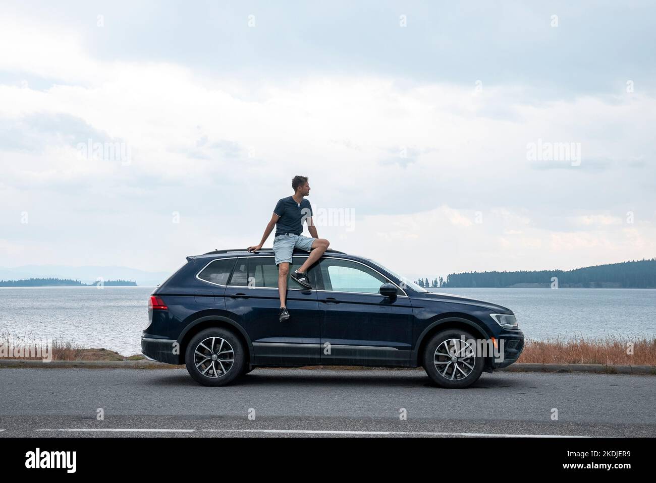 Tourist relaxing on top of car at roadside with sky in background at ...