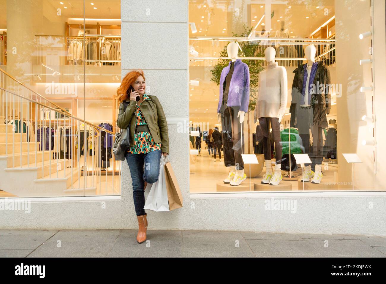 smile adult woman talking on the phone next to a clothing store window ...