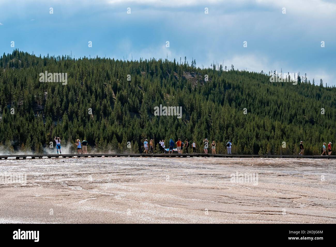 Tourists exploring geyser basin and mountains with cloudy sky in ...