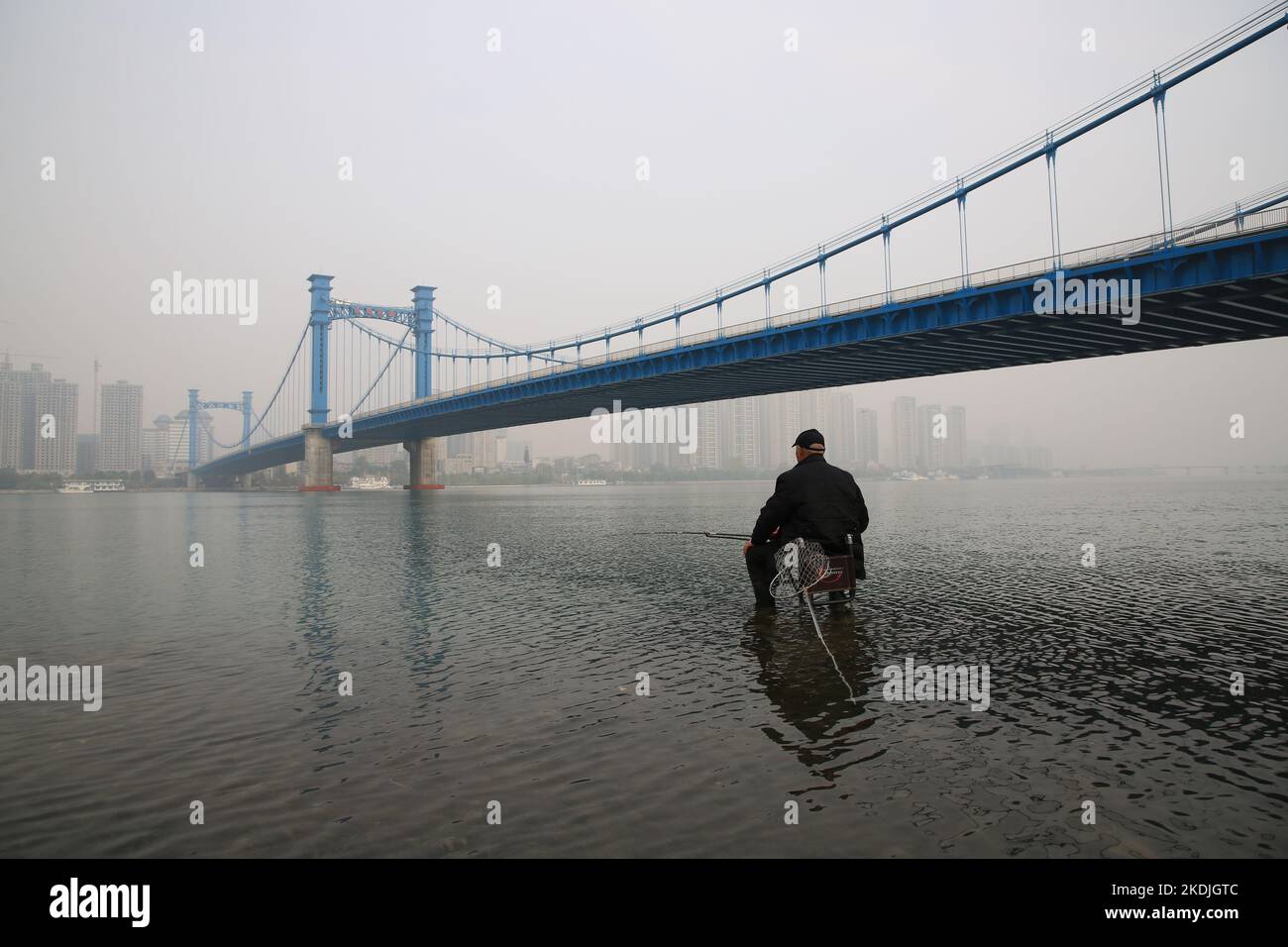 A man is fishing with his seat in the water on "Winter Begins" day of ...